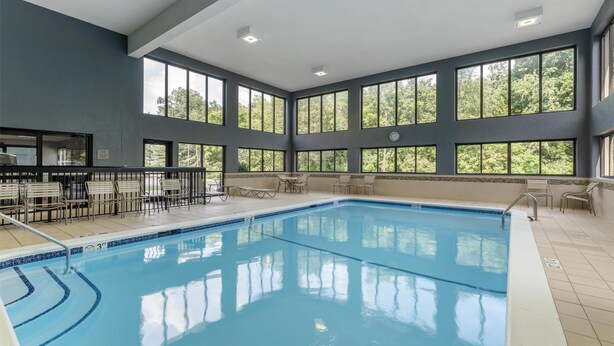 Piscina interior com vista clara para os arredores, incluindo área de estar com cadeiras e vista para o exterior através de grandes janelas.
