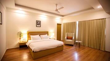 Quarto de hotel com uma cama grande, uma cadeira, uma mesa pequena e um ventilador de teto.