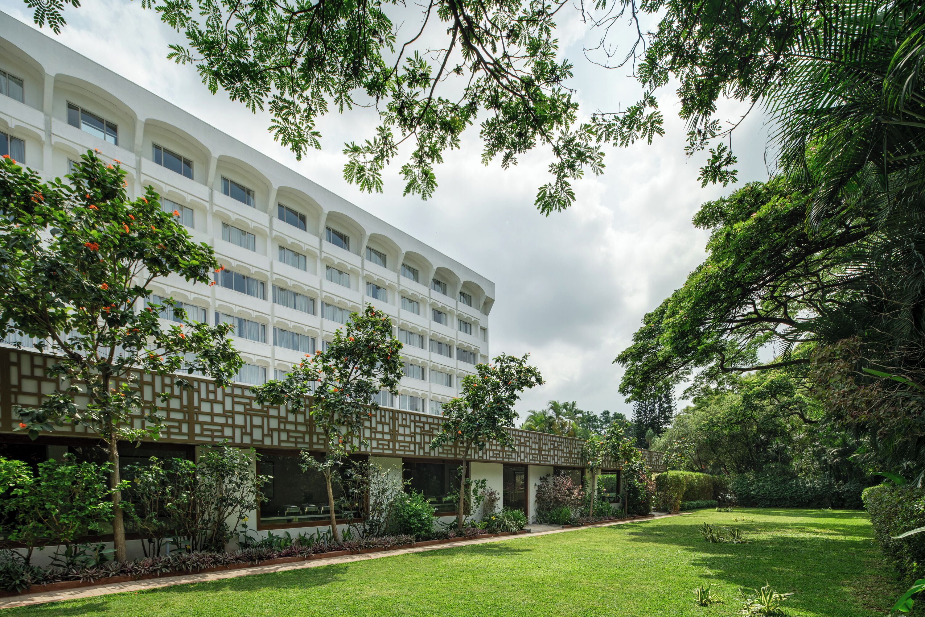 Hotel com design arquitetônico moderno, apresentando um edifício espaçoso com várias janelas e um jardim bem cuidado com diversas plantas e árvores.