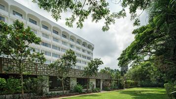 Hotel com design arquitetônico moderno, apresentando um edifício espaçoso com várias janelas e um jardim bem cuidado com diversas plantas e árvores.