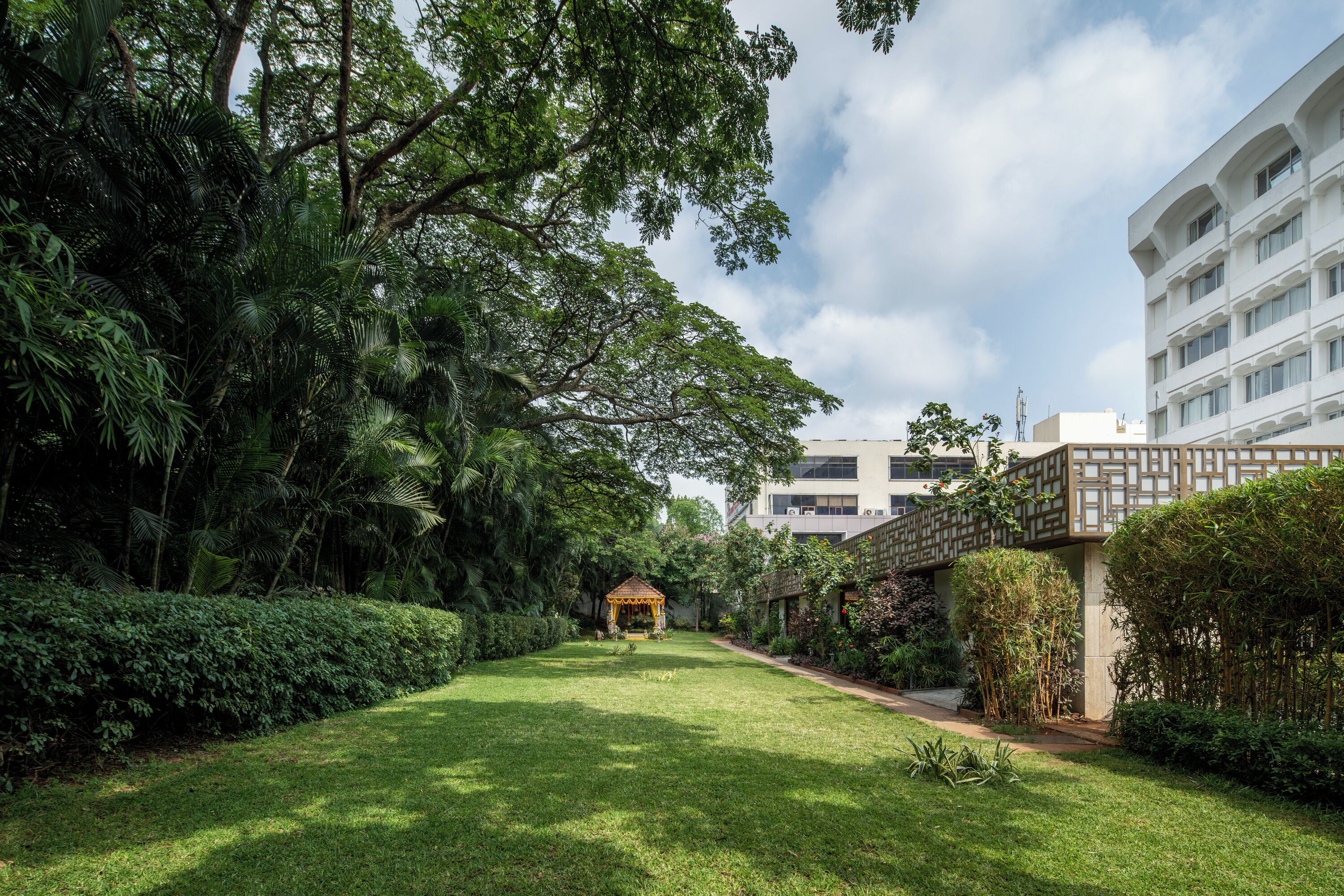 Um jardim exuberante com um gazebo, um caminho e um edifício moderno ao fundo.