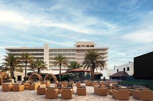 Pátio de hotel com área de estar externa e palmeiras.