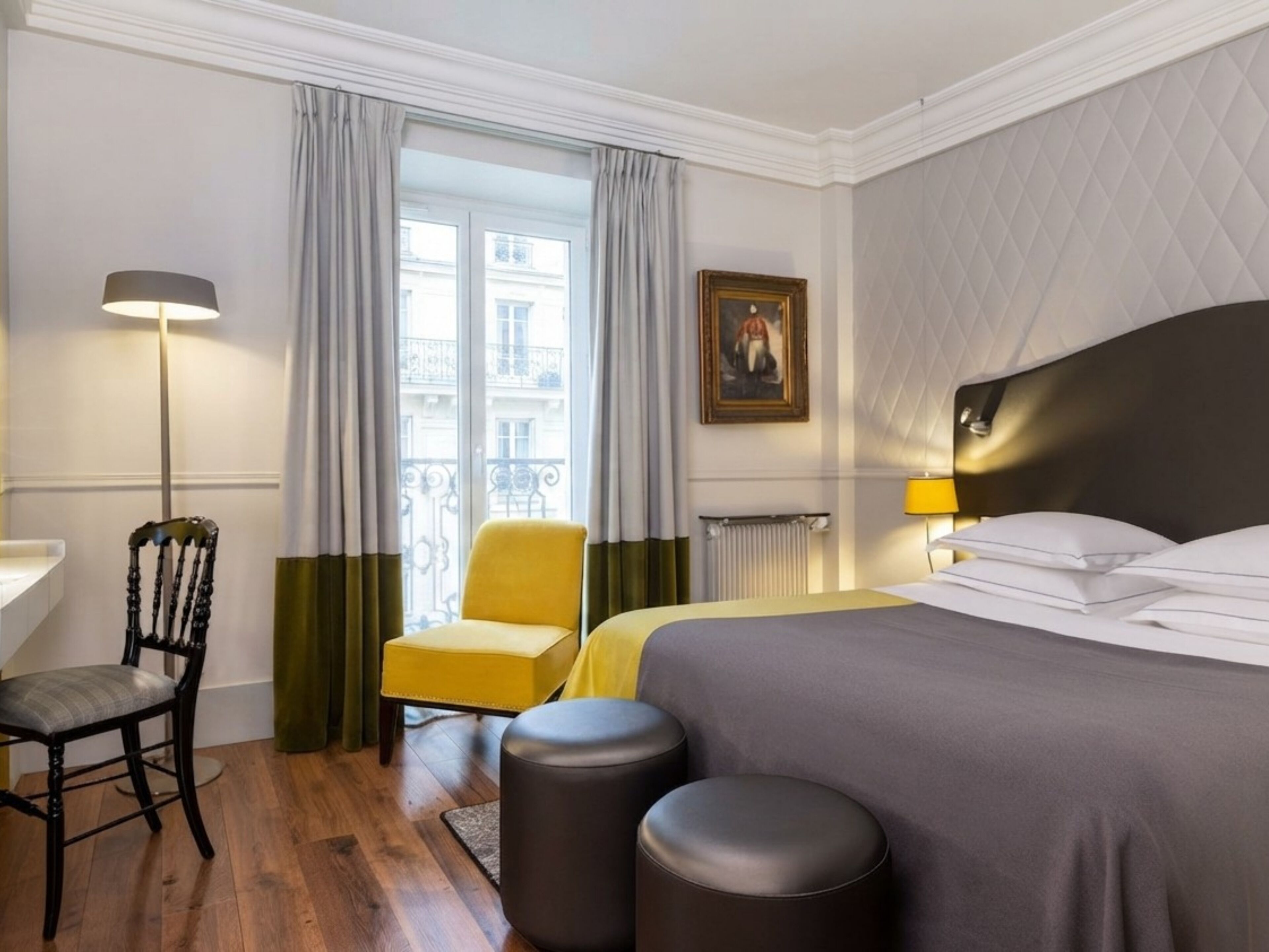 Quarto de hotel com uma cama, uma cadeira, um abajur e uma janela com cortinas.