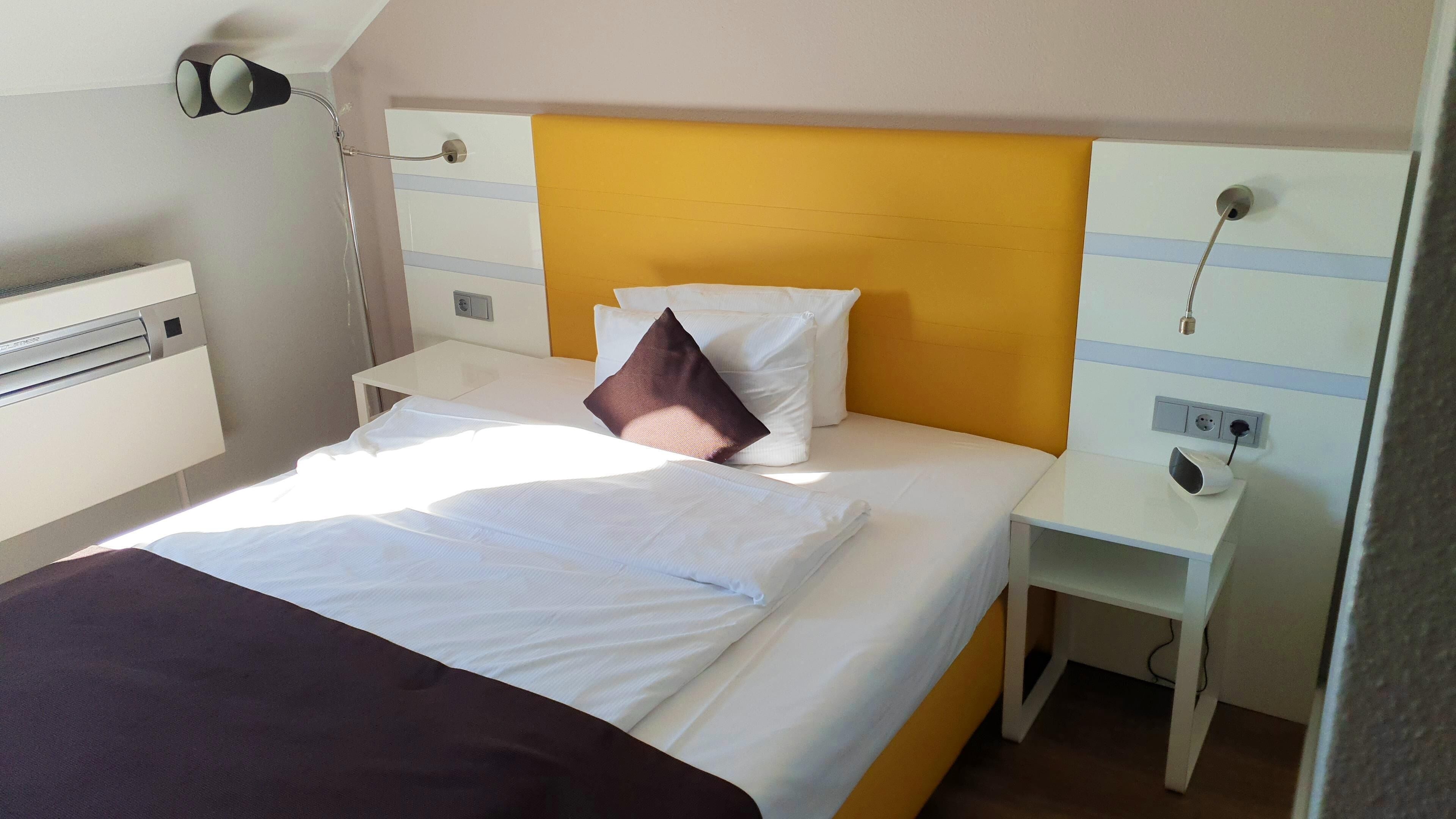 Quarto de hotel com cama, mesas de cabeceira, escrivaninha e luminária.