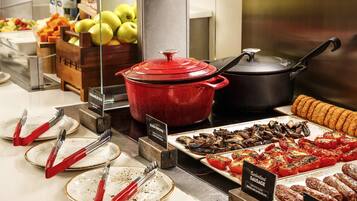 Buffet variado com diversos pratos, incluindo ovos mexidos, batata palha, tomate assado, salsicha Cumberland e bacon frito.