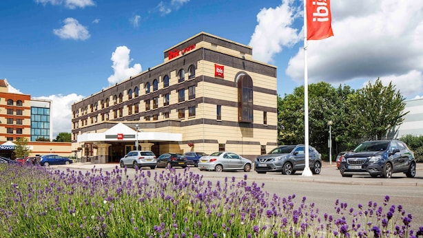 Hotel com fachada moderna, uma bandeira e um estacionamento cheio de carros.