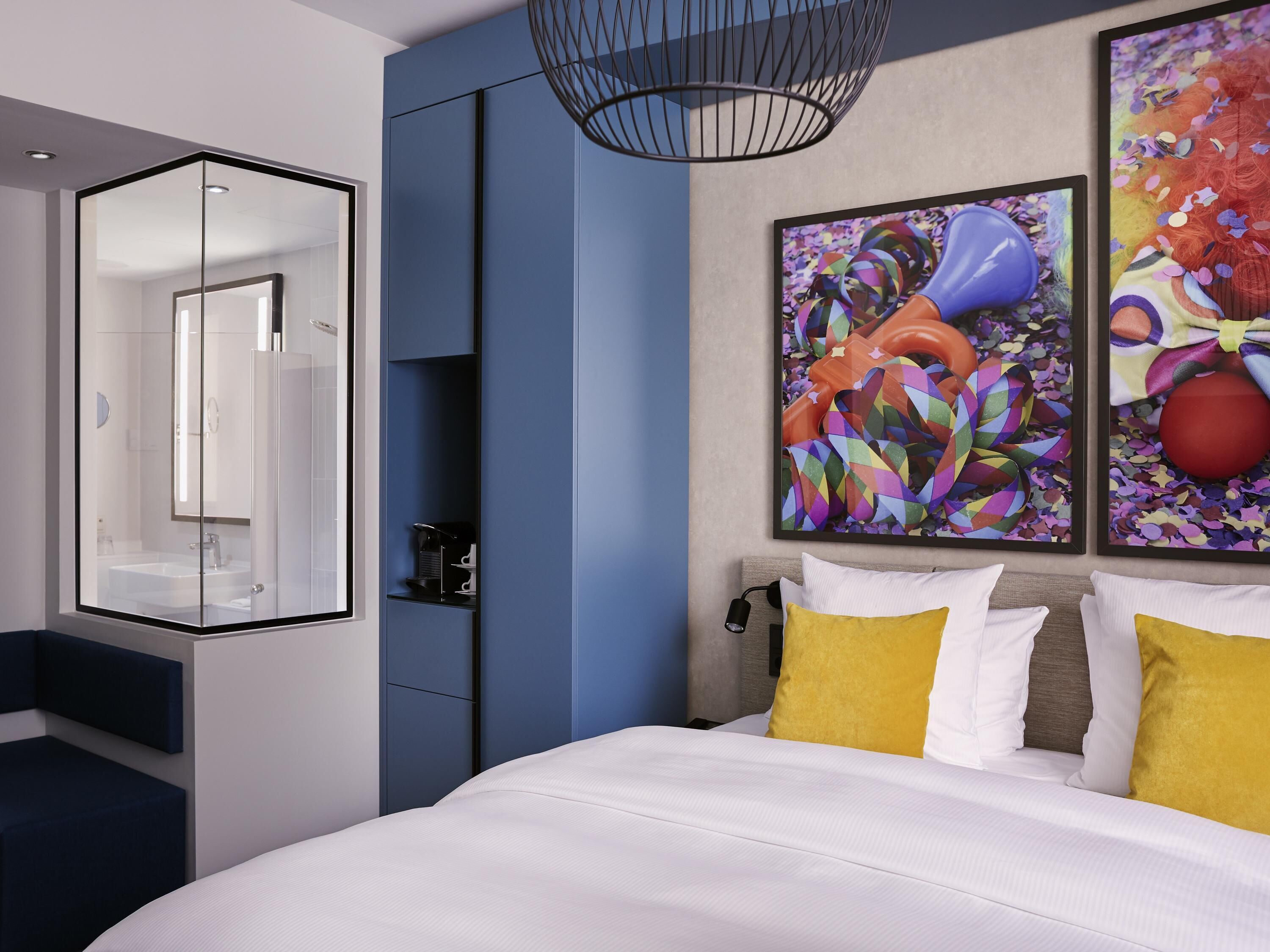 Quarto moderno com cama grande, mesa de cabeceira, espelho e duas pinturas abstratas na parede.