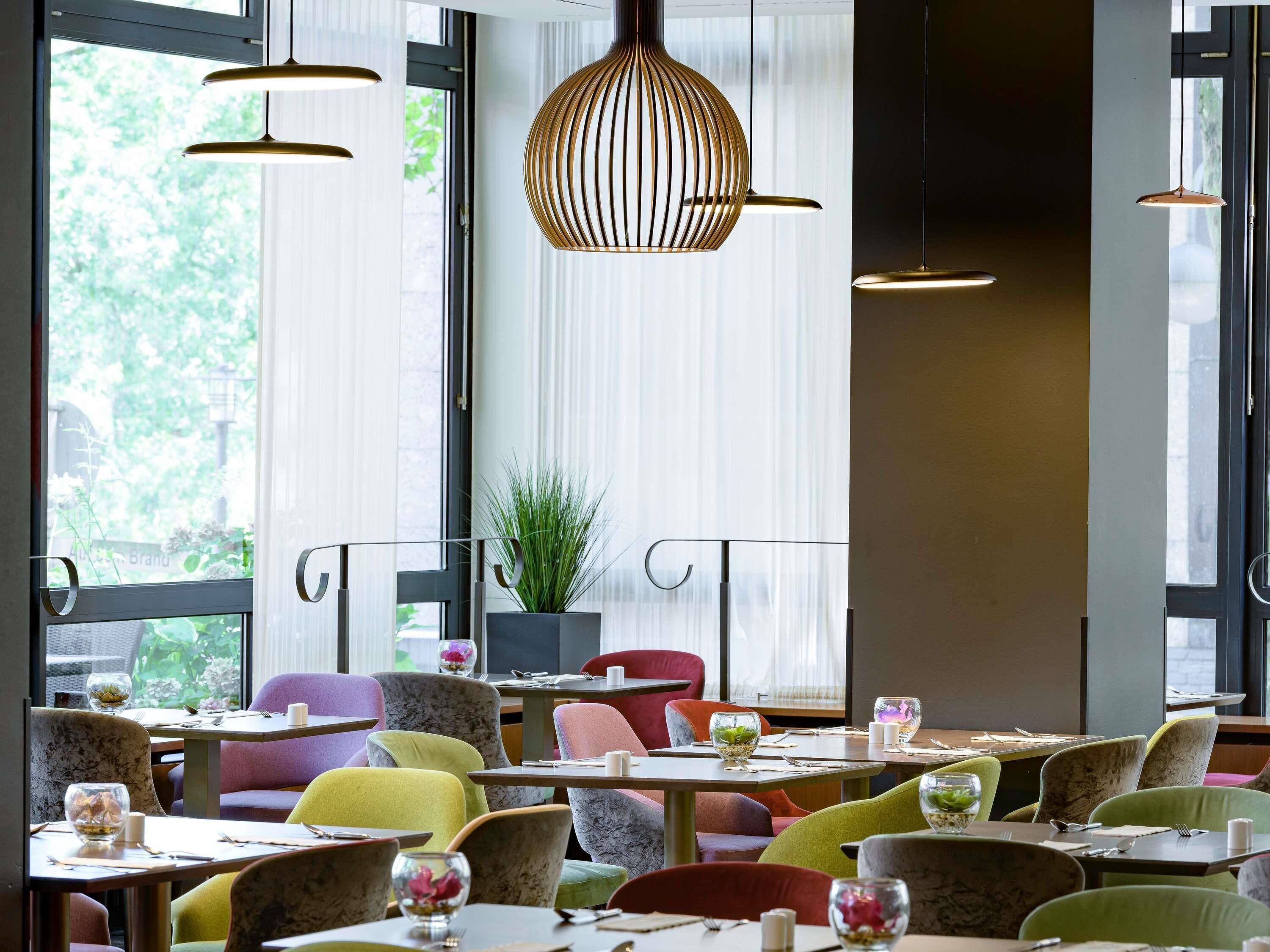 Interior de restaurante com várias mesas, cadeiras e luminárias pendentes.