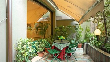 Um pequeno pátio com mesa e cadeiras, rodeado por plantas em vasos e um cercado de madeira.