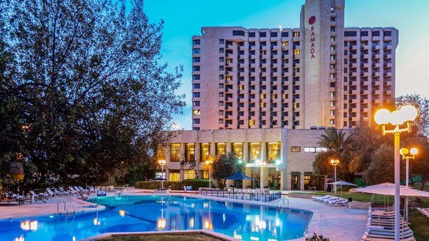 Um hotel com piscina, cadeiras de descanso e um edifício grande ao fundo.