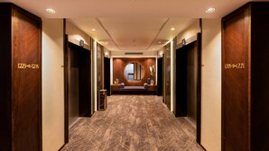 Um corredor de hotel com portas de madeira, um banco e um espelho redondo.