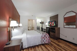 Quarto de hotel com uma cama, televisão, escrivaninha e espelho.