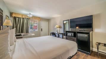 Quarto de hotel com cama, escrivaninha, televisão e um pequeno frigorífico.
