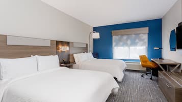 Quarto de hotel com duas camas, uma escrivaninha, uma cadeira e uma televisão.