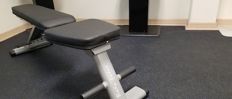 Uma academia com um banco de exercícios preto e máquinas de musculação.