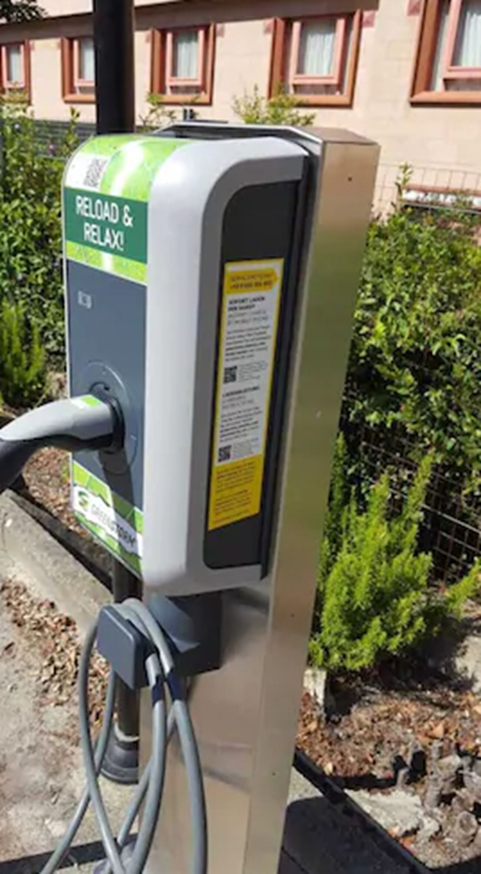 Uma estação de carregamento público para veículos elétricos com uma etiqueta verde e branca que diz 'RELOAD & RELAX!'.
