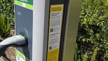 Uma estação de carregamento público para veículos elétricos com uma etiqueta verde e branca que diz 'RELOAD & RELAX!'.