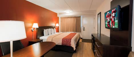 Quarto de hotel com cama, abajures, escrivaninha, televisão e cômoda.