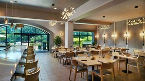 Um restaurante espaçoso com pé-direito alto, janelas amplas e luminárias modernas.