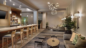 Uma área de bar moderna com banquetas, uma mesa redonda e um sofá numa sala de estar com um tapete estampado.