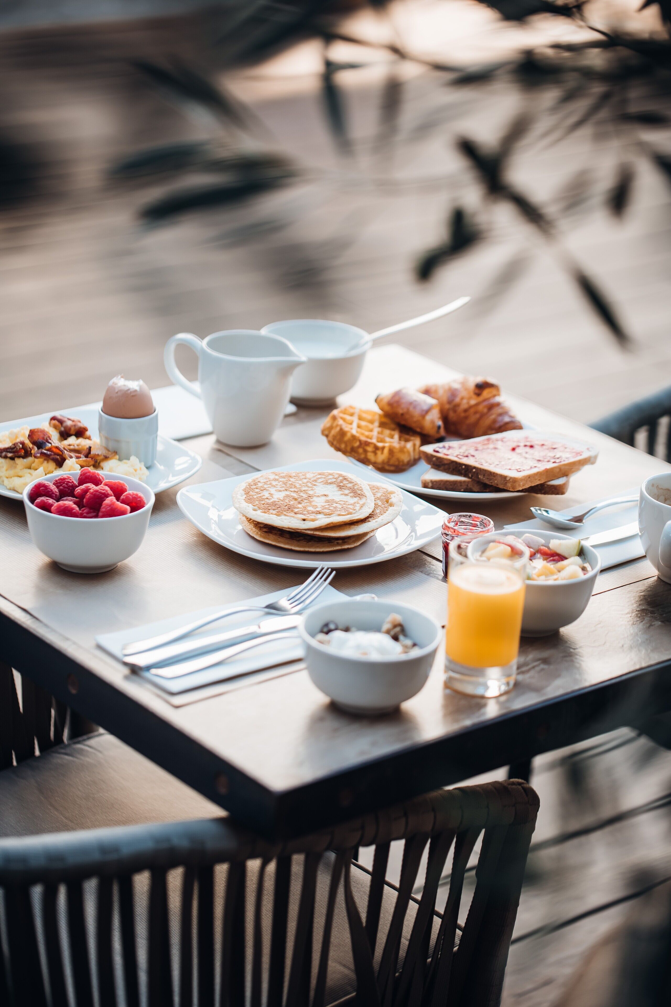 Uma mesa de café da manhã com pratos de comida, uma tigela de frutas, um jarro de suco e uma xícara.