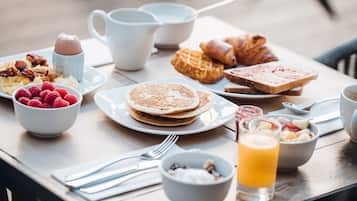 Uma mesa de café da manhã com pratos de comida, uma tigela de frutas, um jarro de suco e uma xícara.