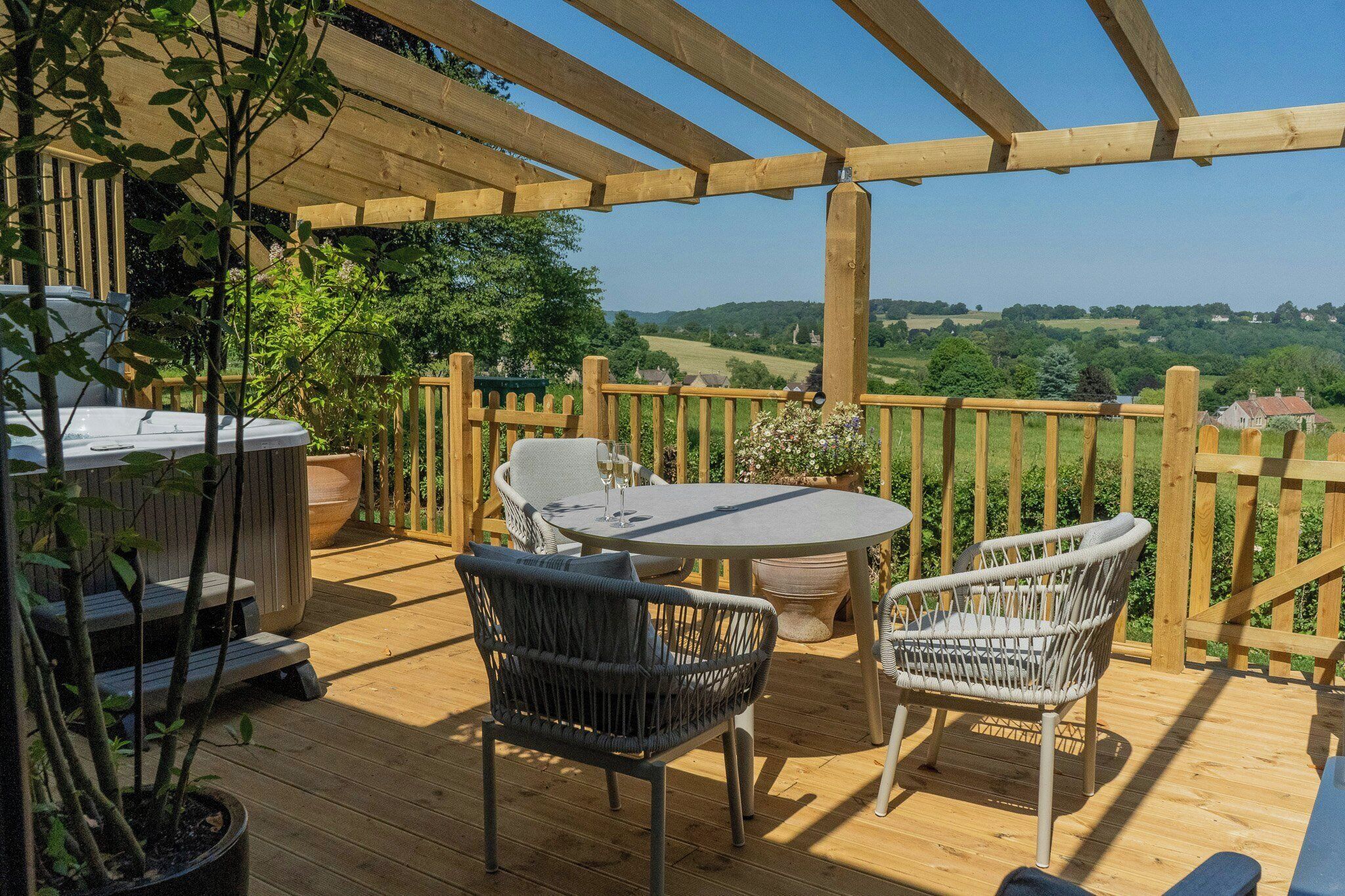 Um deck de madeira com pérgola, área de estar externa e vista para o campo.