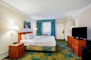 Quarto de hotel com uma cama, televisão, escrivaninha e um quadro na parede.
