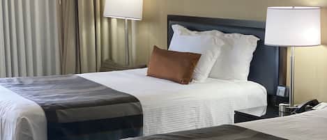 Quarto de hotel com duas camas, uma janela grande com cortinas e duas luminárias de cabeceira.