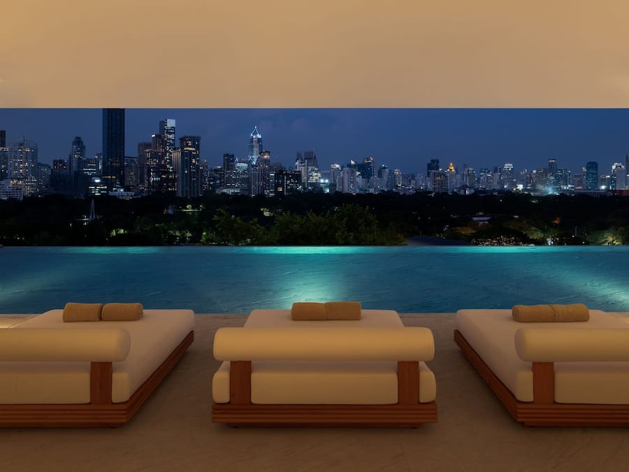 Quarto de hotel moderno com vista para o horizonte da cidade, piscina infinita e três sofás brancos.