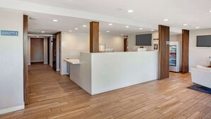 Uma área de recepção com piso de madeira, um balcão de atendimento, um refrigerador e uma televisão de tela plana.