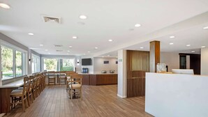 Um hall de hotel espaçoso e moderno, com um balcão de recepção alongado, cadeiras de madeira e uma ampla área de refeições.