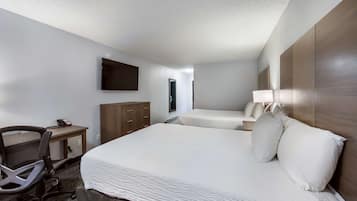 Quarto de hotel com uma cama grande, uma escrivaninha com cadeira, televisão de tela plana na parede e um guarda-roupa de madeira.