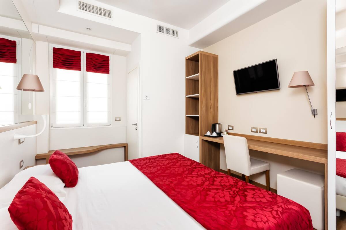 Quarto de hotel com cama, escrivaninha, televisão e guarda-roupa.