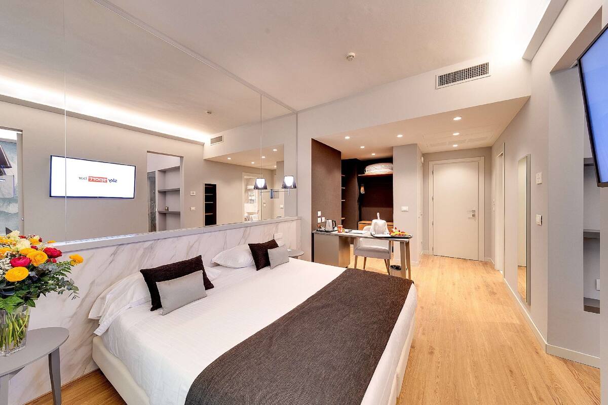 Quarto de hotel moderno com uma cama grande, escrivaninha, cadeira e televisão.