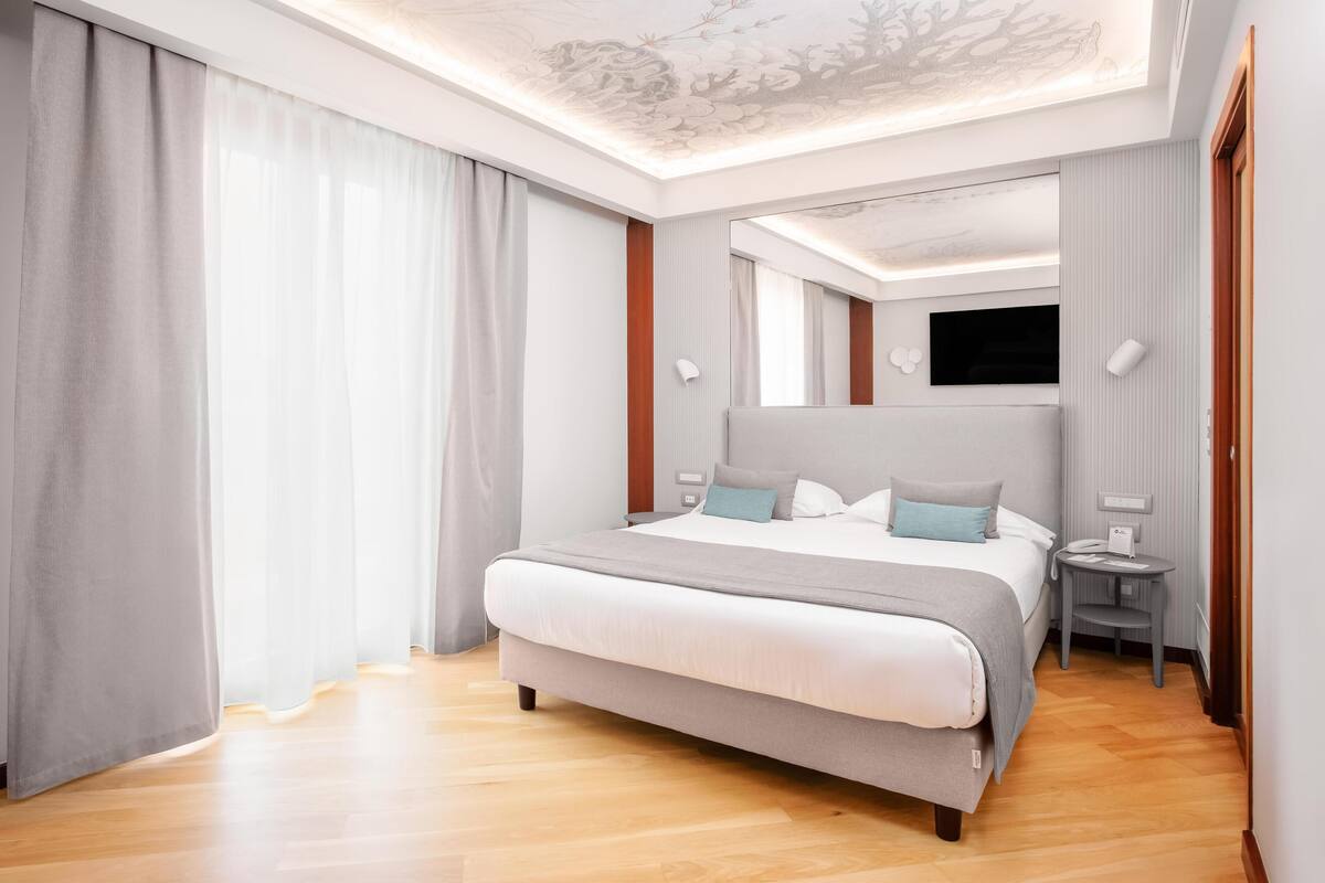 Quarto moderno com uma cama grande, televisão de tela plana montada acima e uma mesinha de cabeceira.