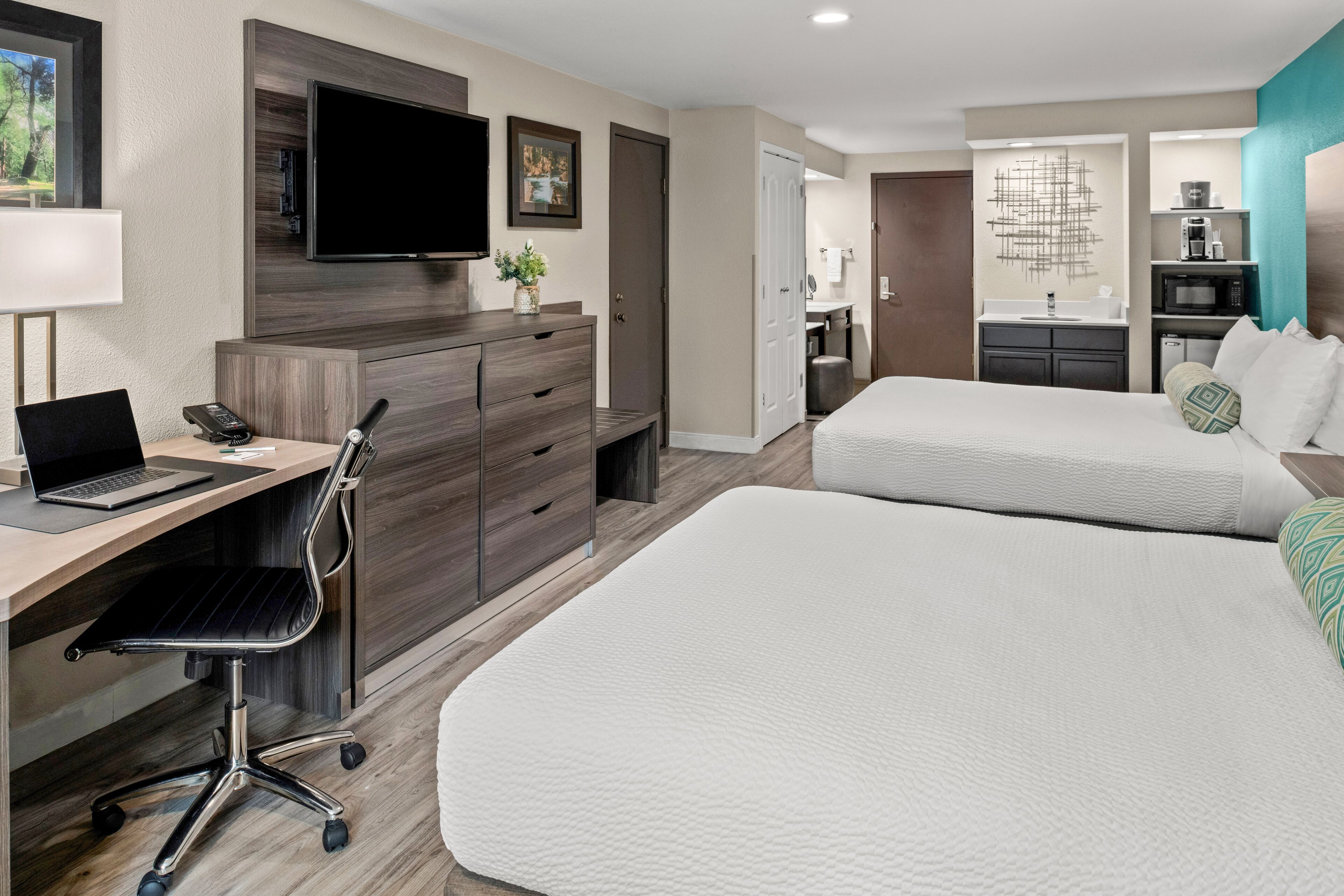 Quarto de hotel com escrivaninha, duas camas, televisão, máquina de café e banheiro.