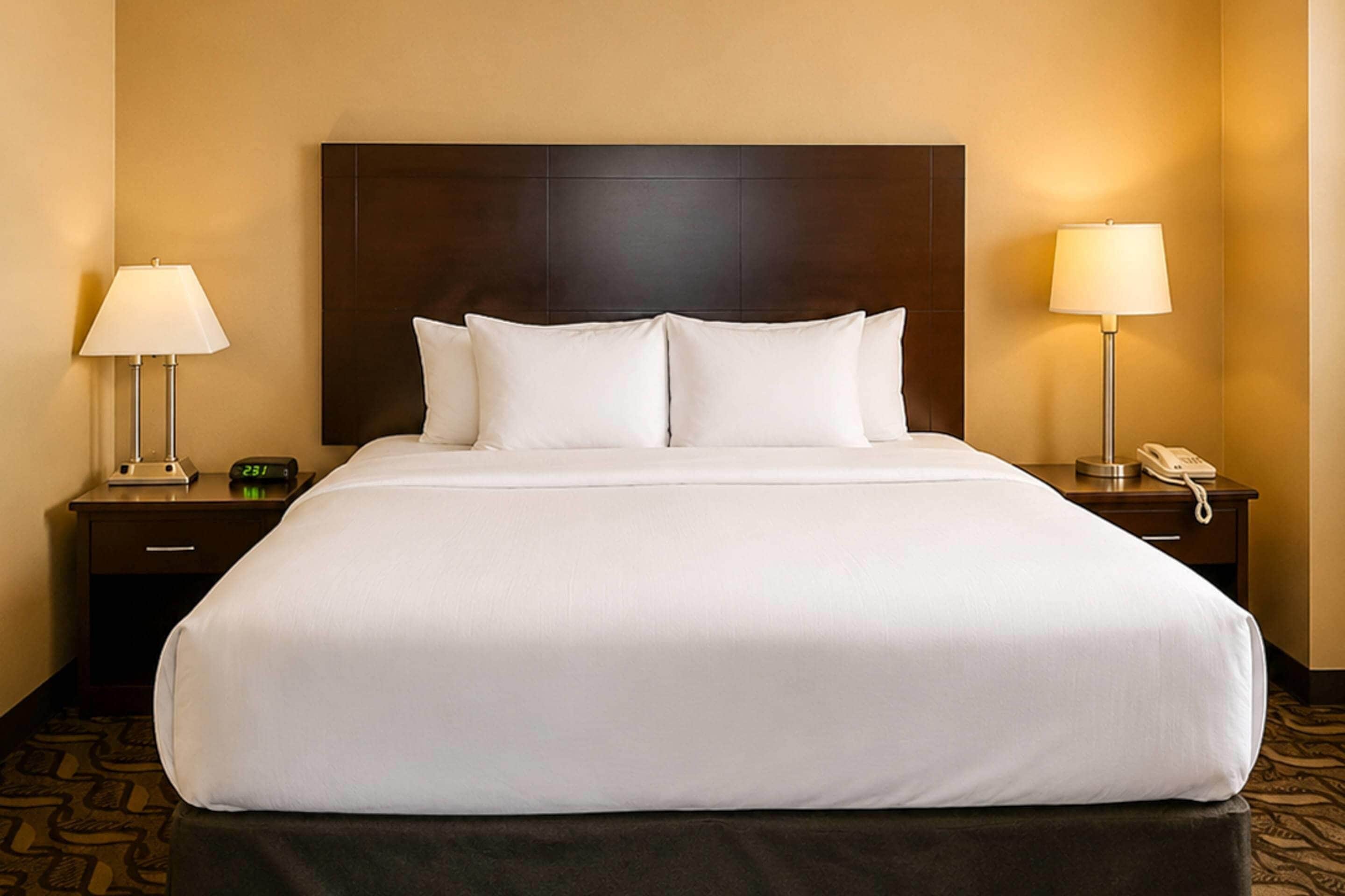 Quarto de hotel com uma cama grande, duas mesas de cabeceira, um criado-mudo, um abajur e um telefone.