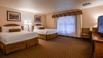 Quarto de hotel com duas camas, uma escrivaninha com cadeira, uma televisão e duas luminárias.