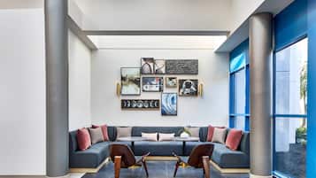 Um interior moderno com um sofá cinzento, duas cadeiras de madeira e uma parede decorada com obras de arte emolduradas.