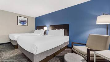 Quarto de hotel com duas camas, uma escrivaninha, uma cadeira, uma luminária e um quadro na parede.