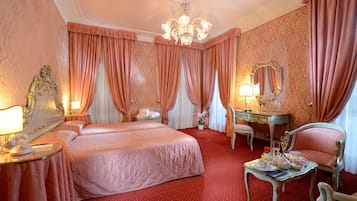 Quarto de hotel com duas camas, uma toucador com espelho, uma mesa de jantar posta para o café da manhã e um candelabro.