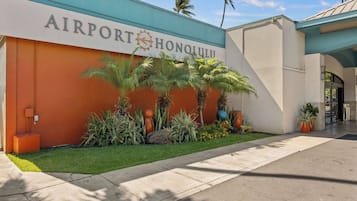 Exterior do edifício do Aeroporto Honolulu, com uma placa, palmeiras e um gramado bem cuidado.