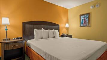 Quarto de hotel com uma cama grande, duas mesas de cabeceira com luminárias, um quadro na parede e um termostato.