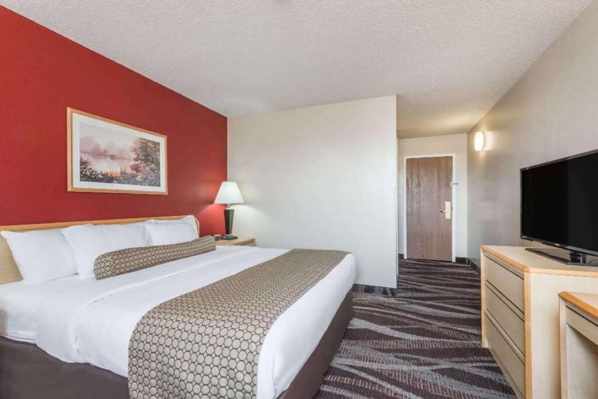 Quarto de hotel com cama, televisão, escrivaninha e porta que dá para outro espaço.