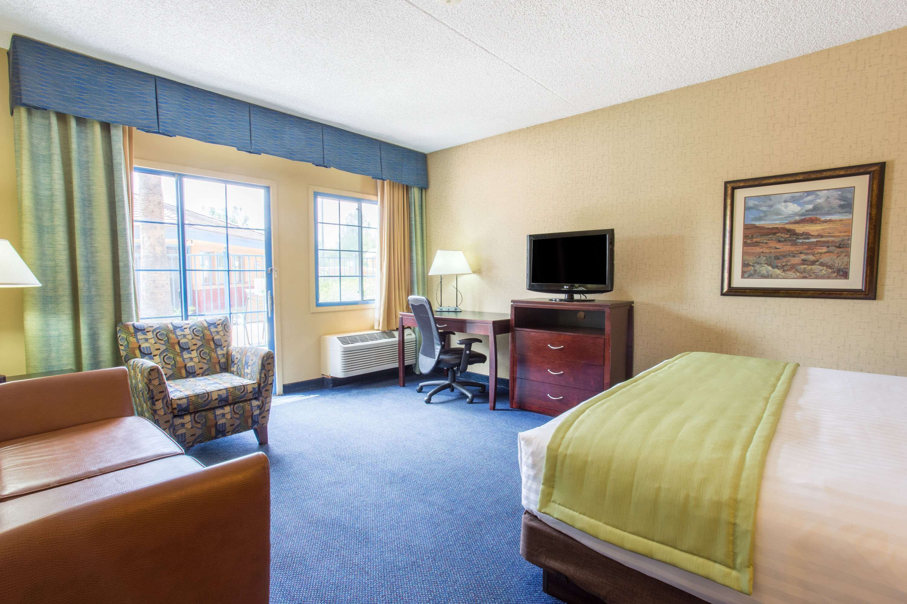 Quarto de hotel com cama, escrivaninha com computador, cadeira e televisão.