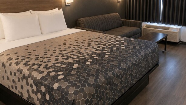 Quarto de hotel com cama, sofá, escrivaninha e janela com cortinas.