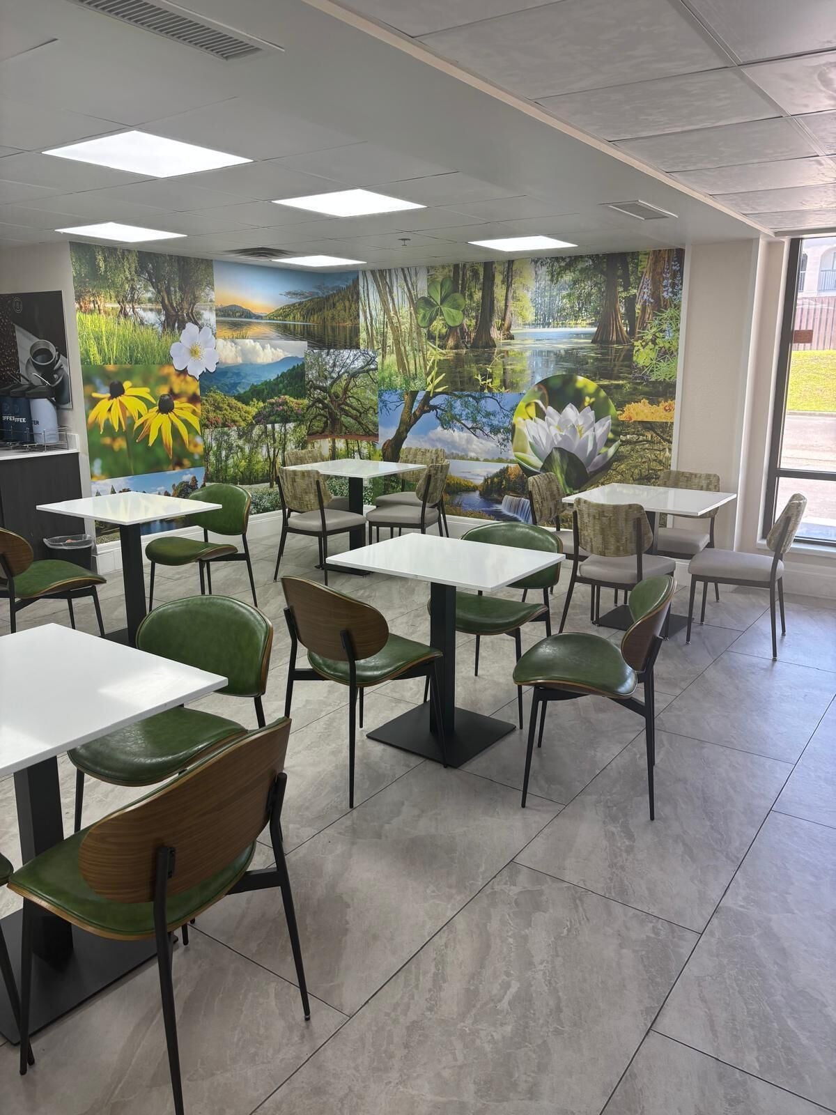 Interior de restaurante com várias mesas e cadeiras, um mural na parede e vista para o exterior.