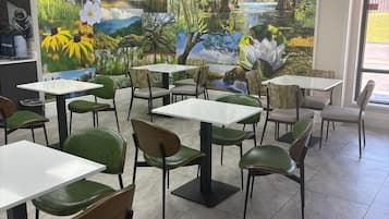 Interior de restaurante com várias mesas e cadeiras, um mural na parede e vista para o exterior.
