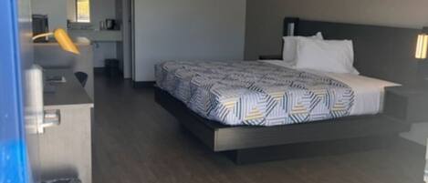 Quarto de hotel moderno com uma cama grande, uma escrivaninha e uma área de kitchenette.